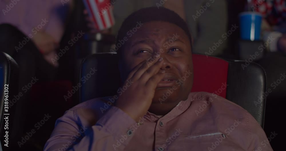 Young guy watching sad drama movie in cinema and wiping tears. Fat man ...