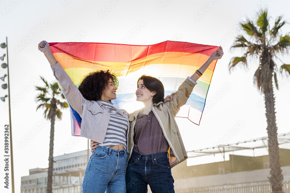young lesbian couple smiling under a rainbow flag Stock Photo | Adobe Stock