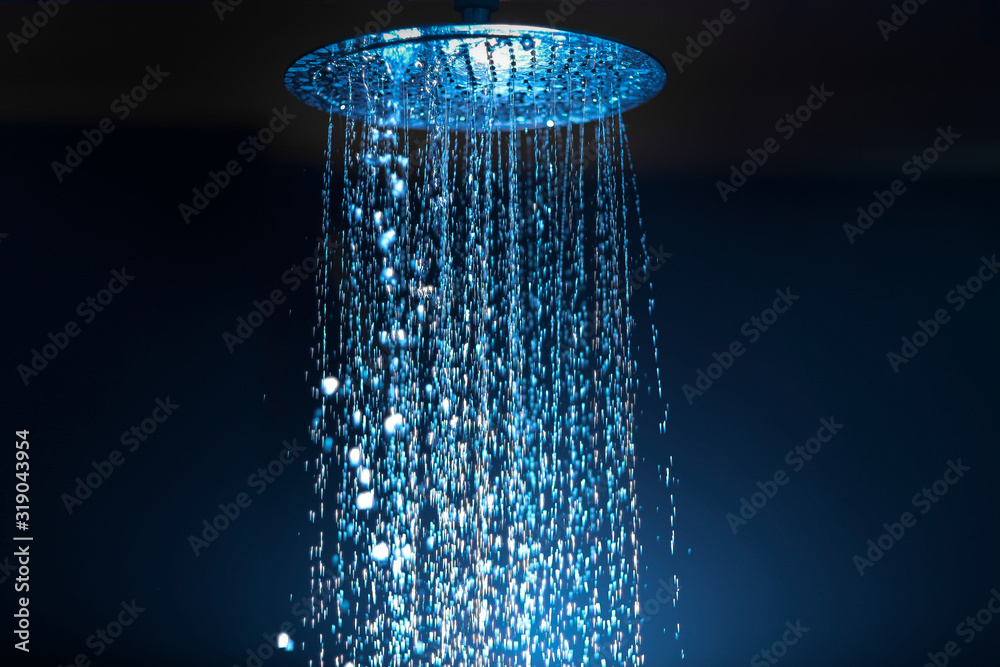Water falling from the shower on a dark background with blue backlight ...