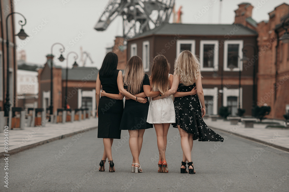 four girls in dresses hug and stand with their backs against the ...