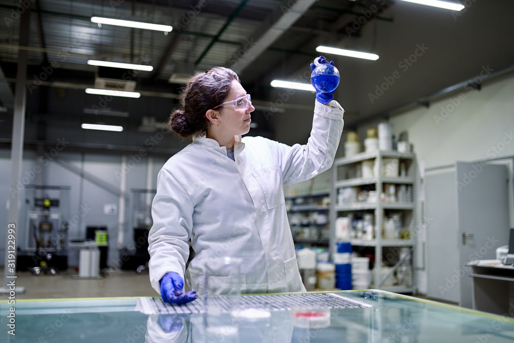 Laboratory woman in white lab coat with flask with blue liquid in her ...
