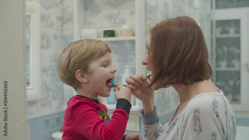 Young mother helps preschool boy in red pajamas with brushing teeth ...