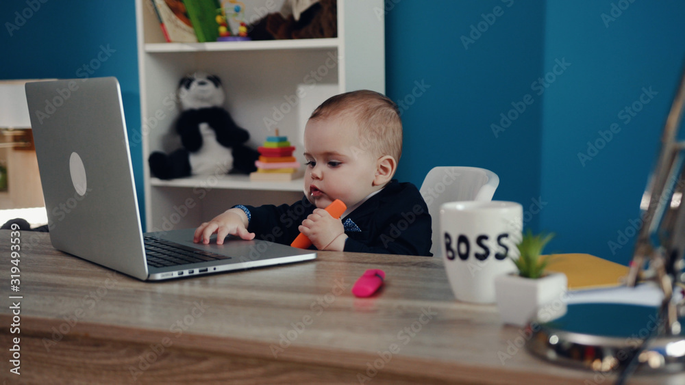 Adorable boss baby working hard by the laptop with notepad and ...