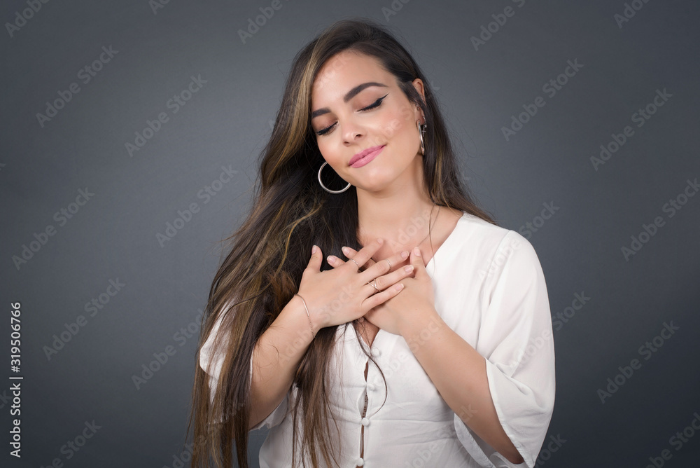 Faithful woman closes eyes and keeps hands on chest near heart, shows ...