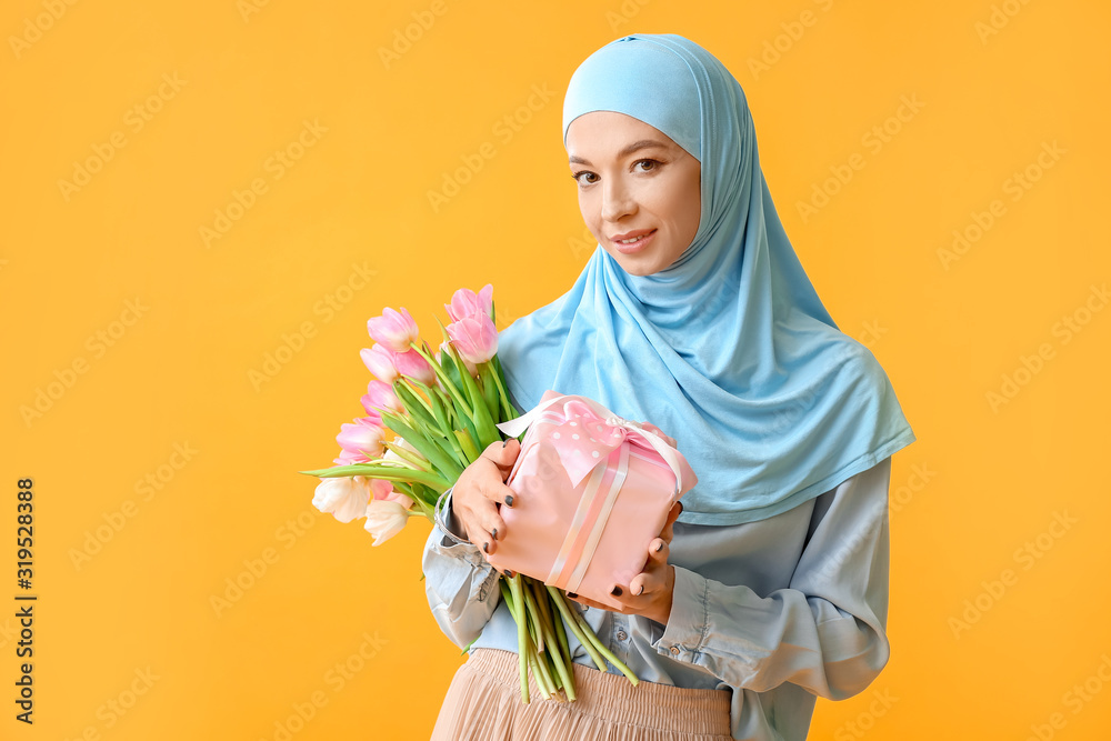 Beautiful Muslim woman with flowers and gift on color background ...
