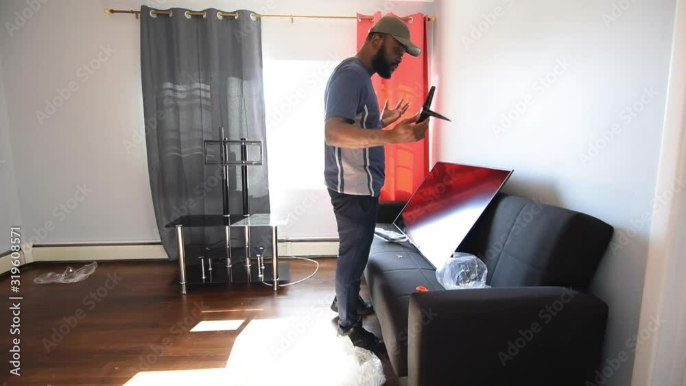 An african american man setting up his TV set in his apartment. A young ...