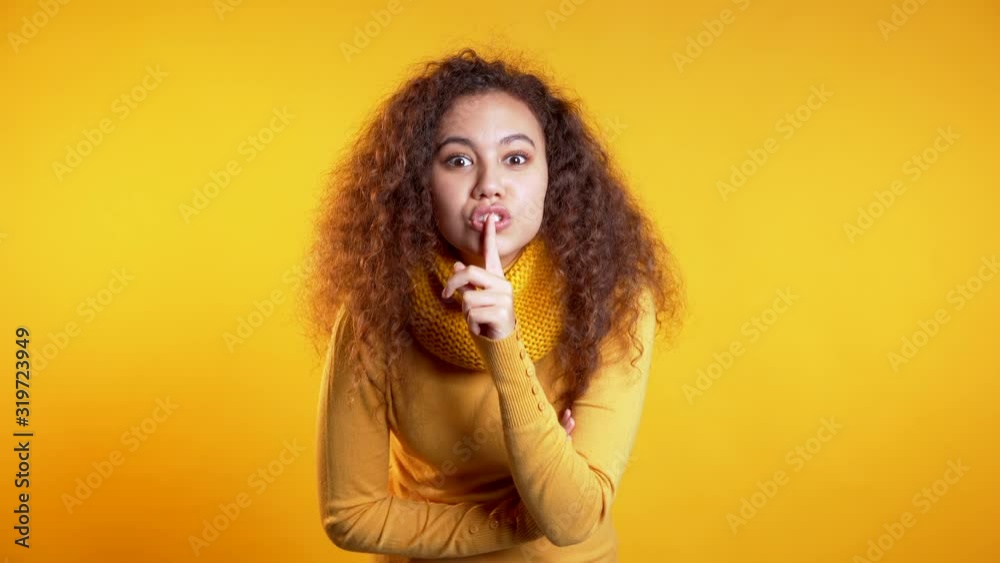 Positive girl holding finger on her lips over yellow background ...