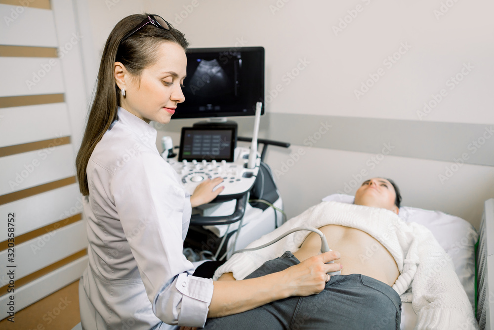 Pretty female doctor operating modern ultrasound scanner while ...