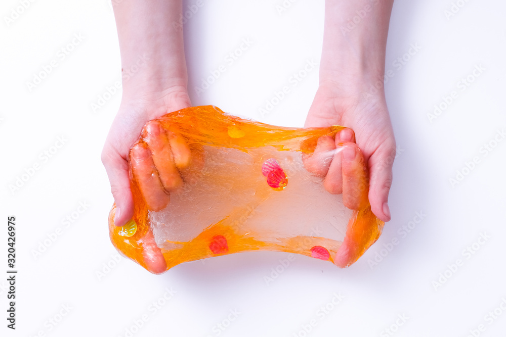 Girl stretching colorful orange slime to the sides. Kids hands playing ...