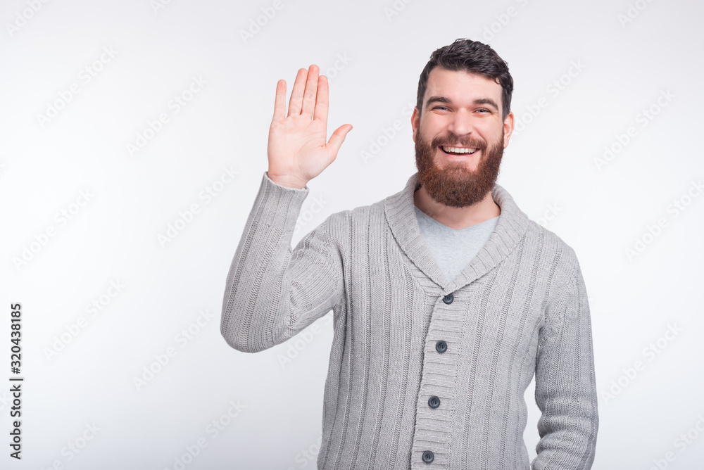 Cheeerful young bearded man is saying hi making hello gesture, and ...