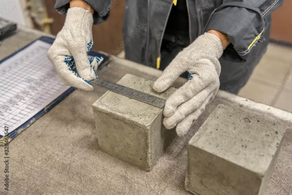 Lab technician measures the size of a concrete cube using a metal ruler ...