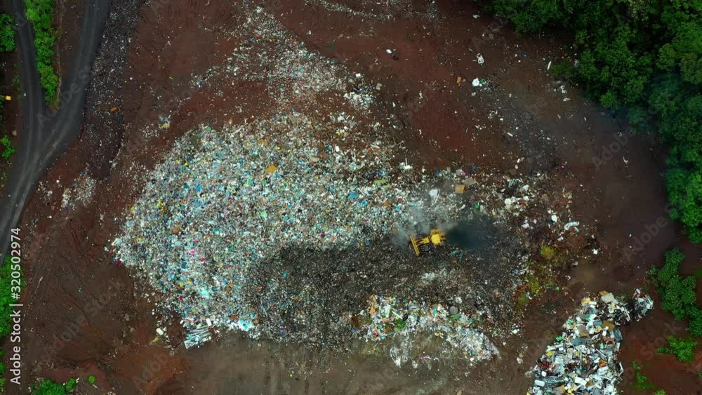 Open landfill in a forest. A bulldozer compacts garbages and plastic ...