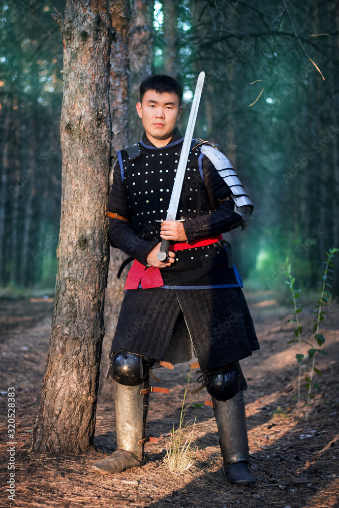 Warrior in black armor with a sword in his hands is leaning against a ...