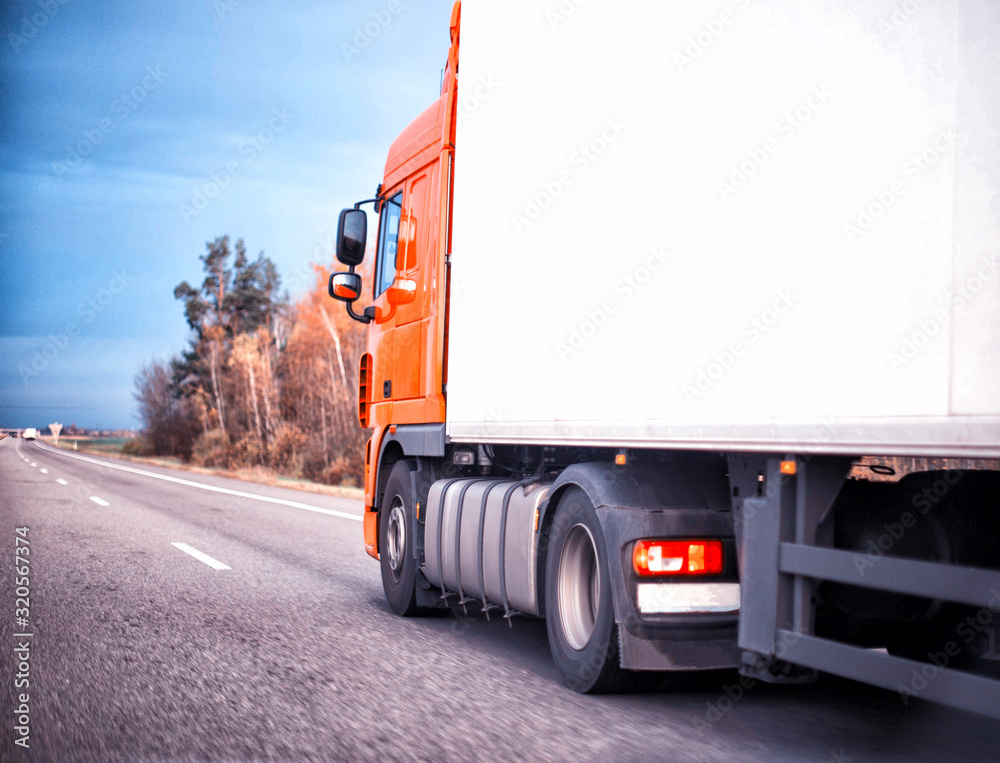An orange truck is transporting goods in a refrigerated trailer on a ...