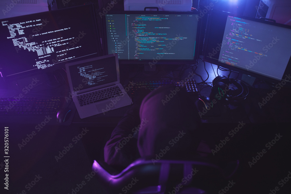 Top view at unrecognizable cyber security hacker wearing hood while working on programming code ...