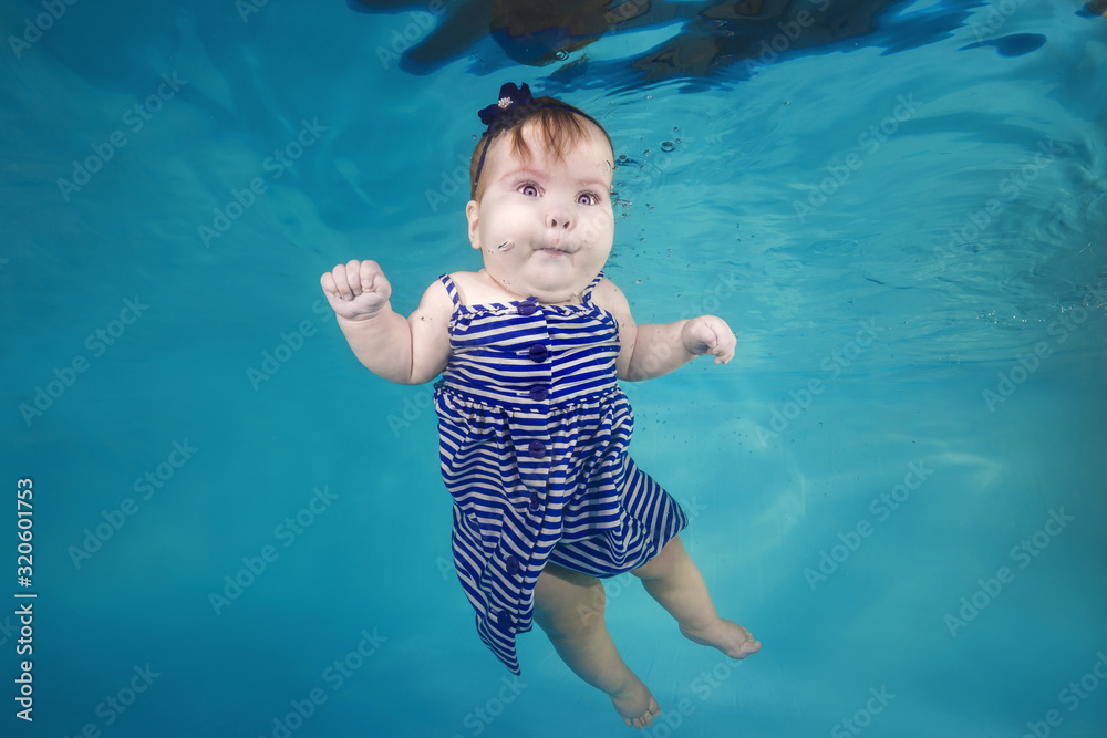 Cute chubby little girl in a sundress dives underwater in a swimming ...