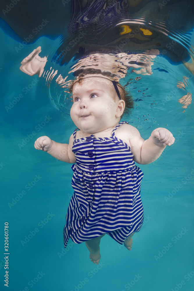 Cute chubby little girl in a sundress dives underwater in a swimming ...
