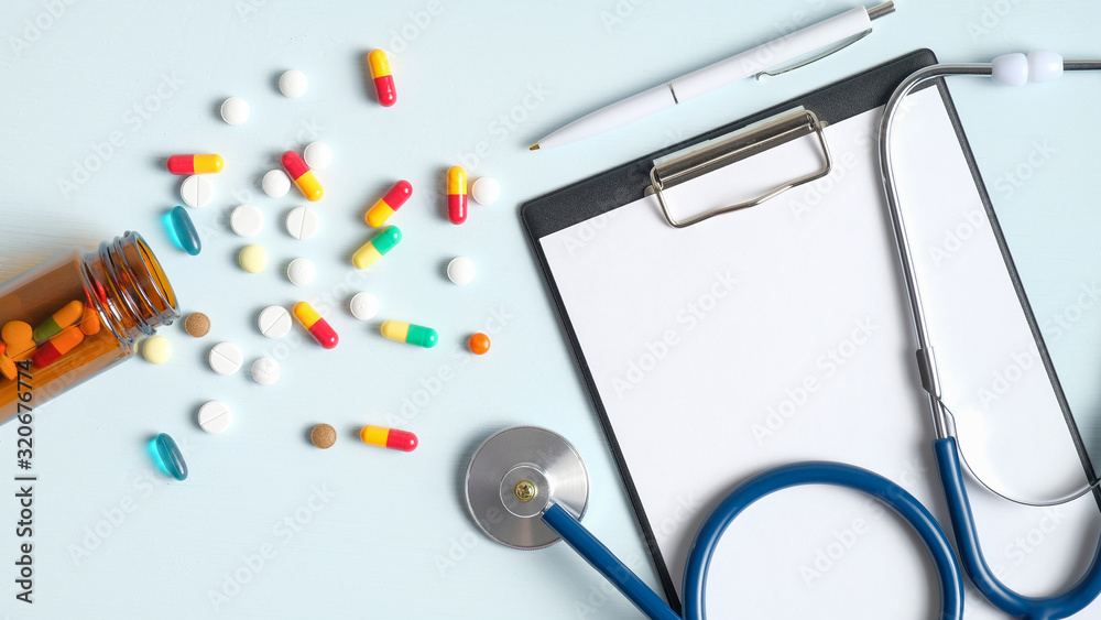 Doctors table with medical clipboard, stethoscope, tablets and pills ...
