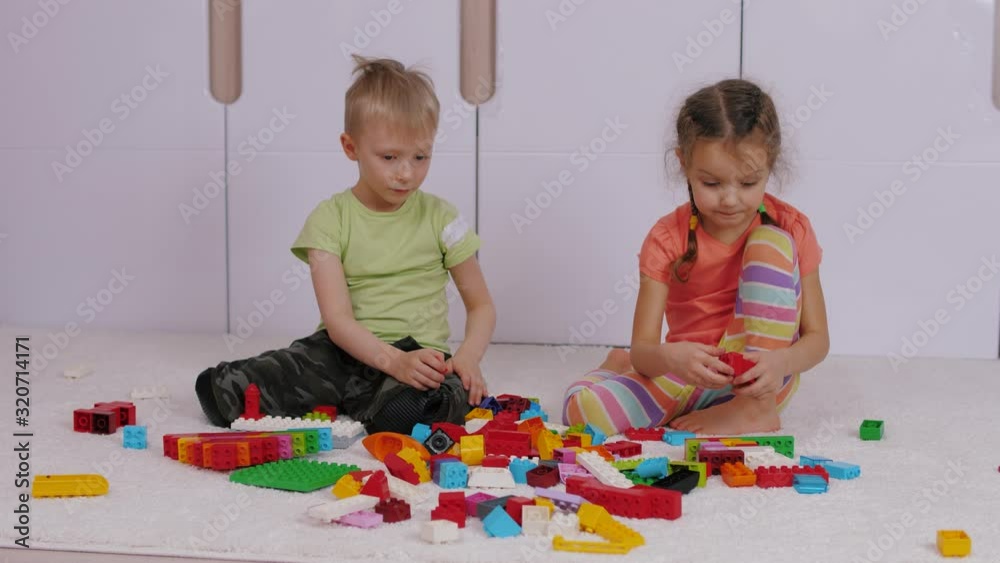 Cute girl and boy are sitting on carpet on floor and playing with ...