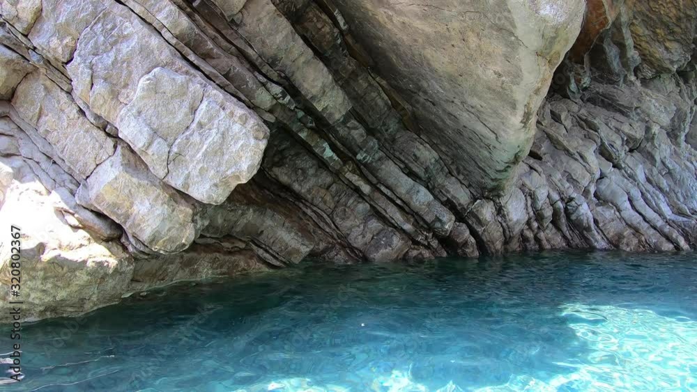 Layered rocks and bright clear sea water in cave, sunlight reflections ...