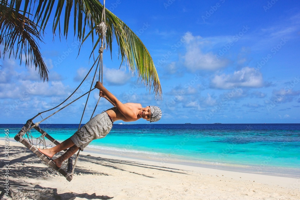 Happy little cute eight year old boy is swinging on coconut palm tree ...
