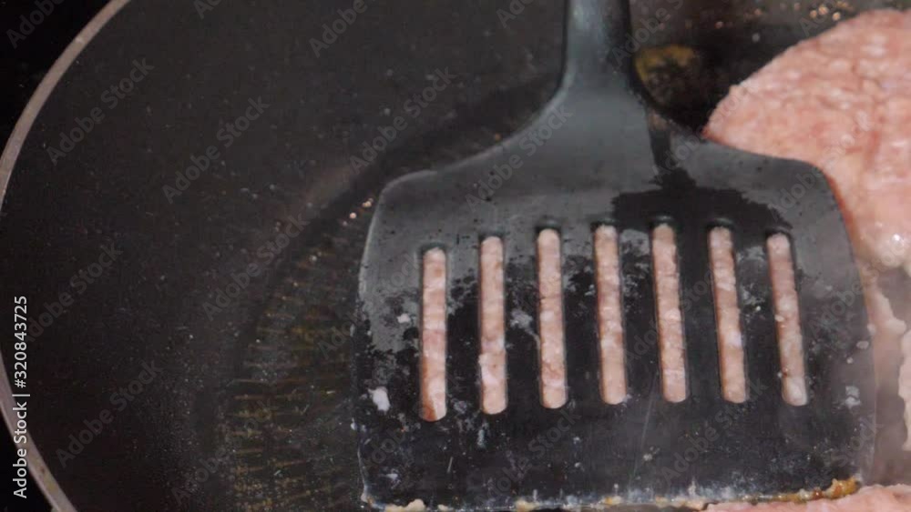 Close up of using a spatula to push down on a beef burger patty so it ...