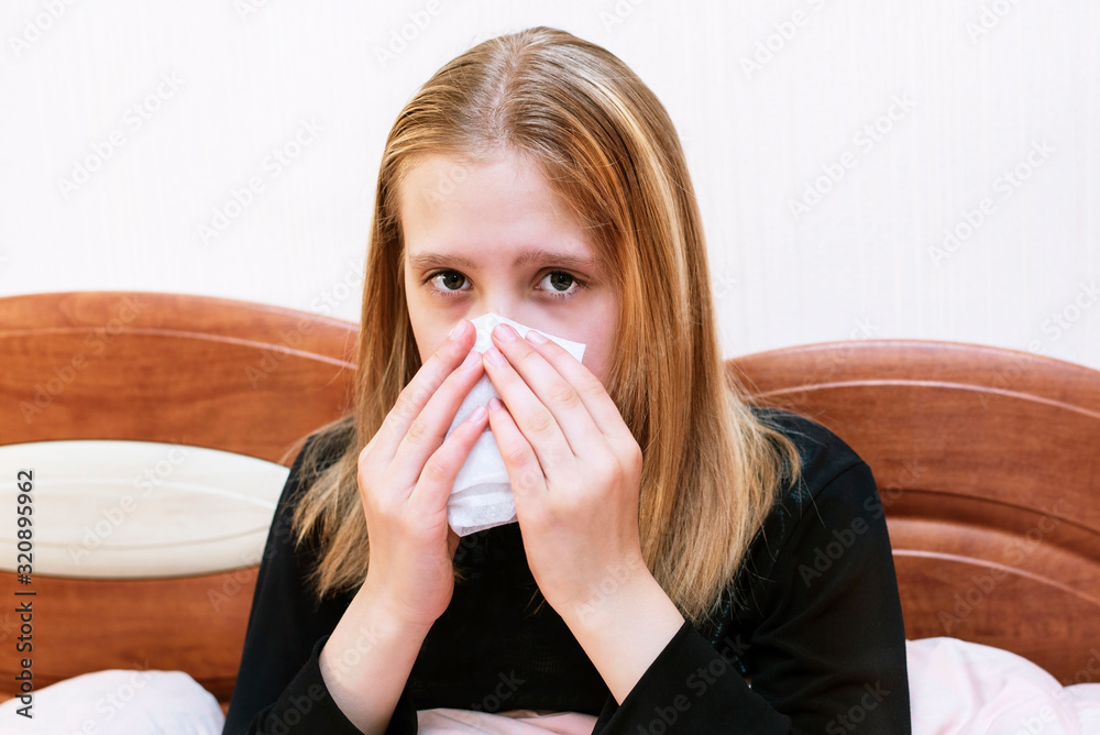 A teenage girl gets sick, lies down at home and wipes her nose with a ...