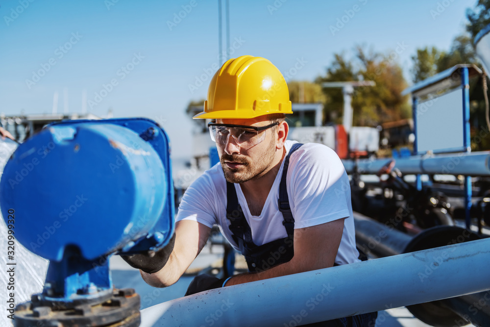 Handsome serious caucasian workman in overalls and with helmet on head ...
