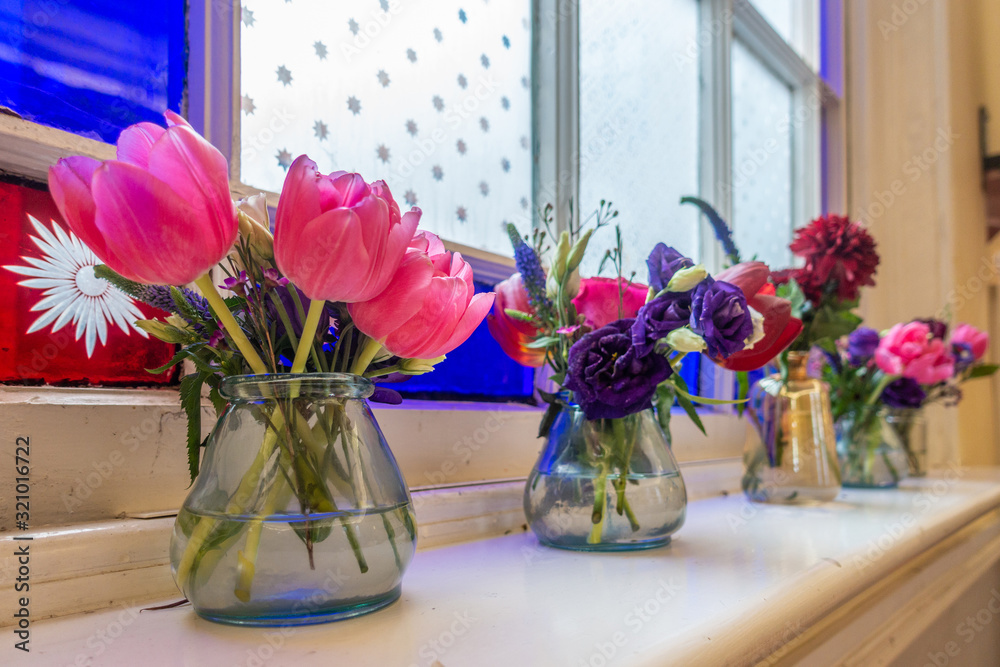 Cut flowers in glass vases on a window sill in front of a stained glass ...
