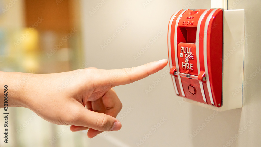 Male hand pointing at red fire alarm switch on concrete wall in office ...