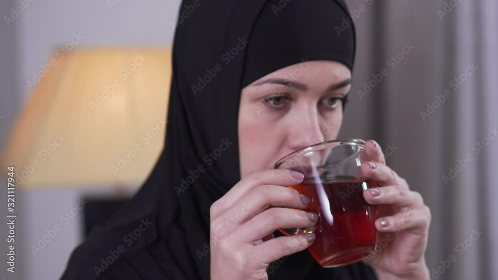 Camera following cup of tea in female hands. Charming serious Muslim ...