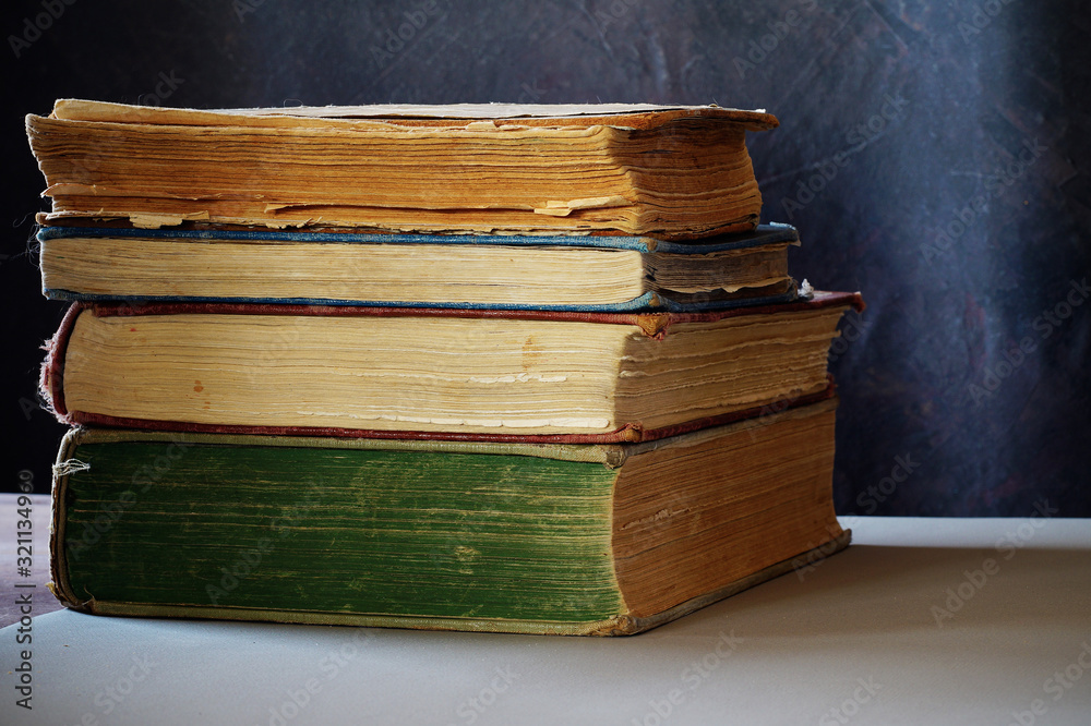 Four books of different sizes and colors are stacked on top of each ...
