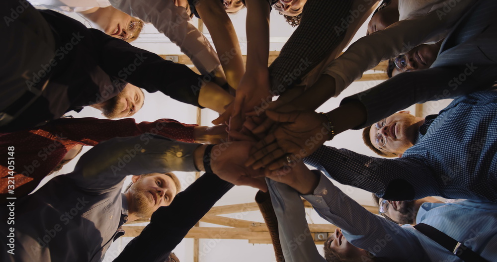 Low angle close-up, happy group of diverse business people put hands together. Teamwork at ...