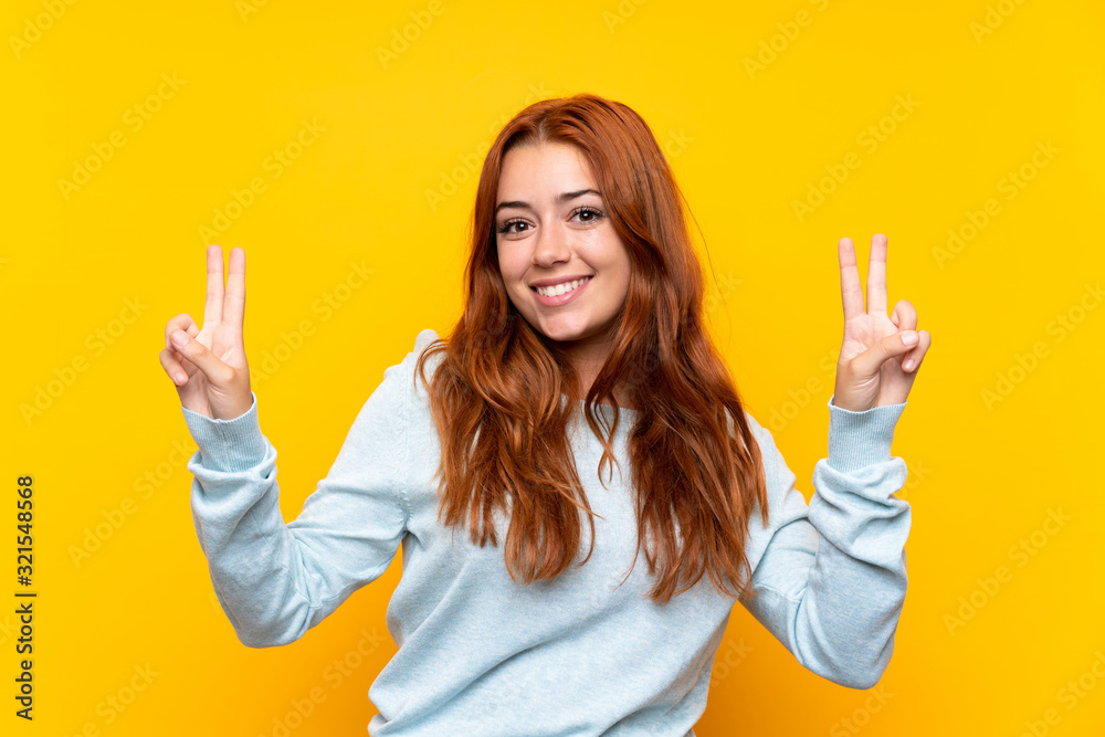 Teenager redhead girl over isolated yellow background showing victory ...