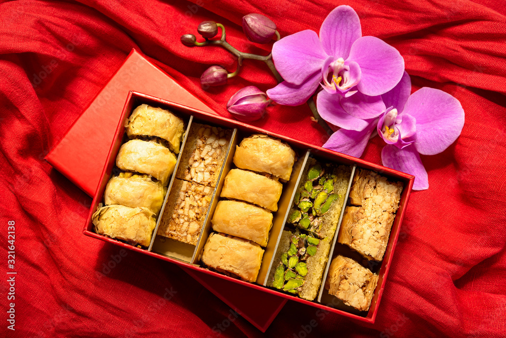 Eastern sweets. Baklava in a red box and an orchid branch on a red ...