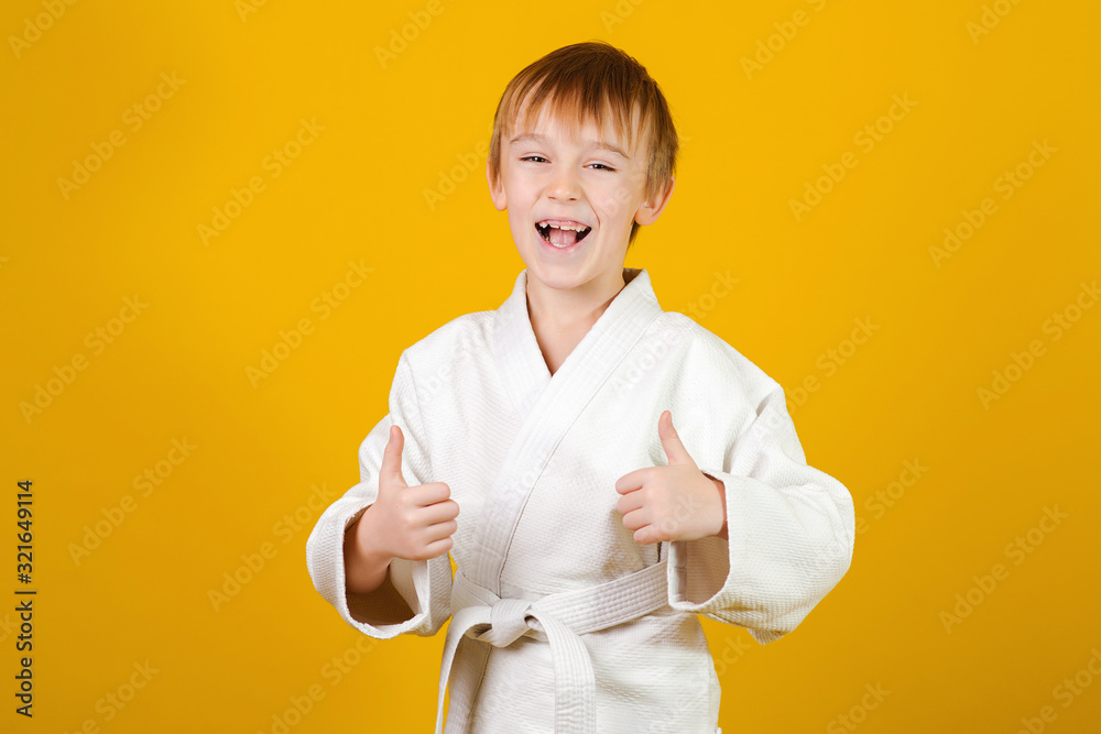 Smiling happy boy in a white kimono. Sporty kid on a yellow background ...