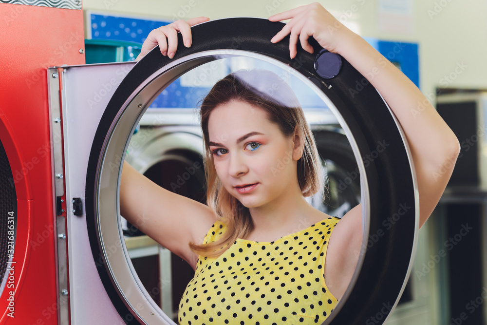 Beautiful young woman is sitting on the floor near washing machine ...