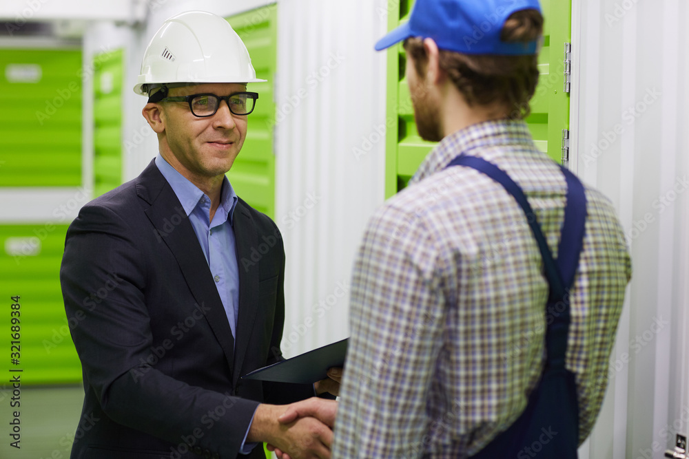 Confident businessman in suit and in work helmet shaking hand to manual ...