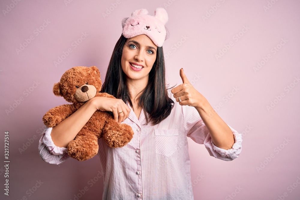 Young brunette woman with blue eyes wearing pajama hugging teddy bear ...