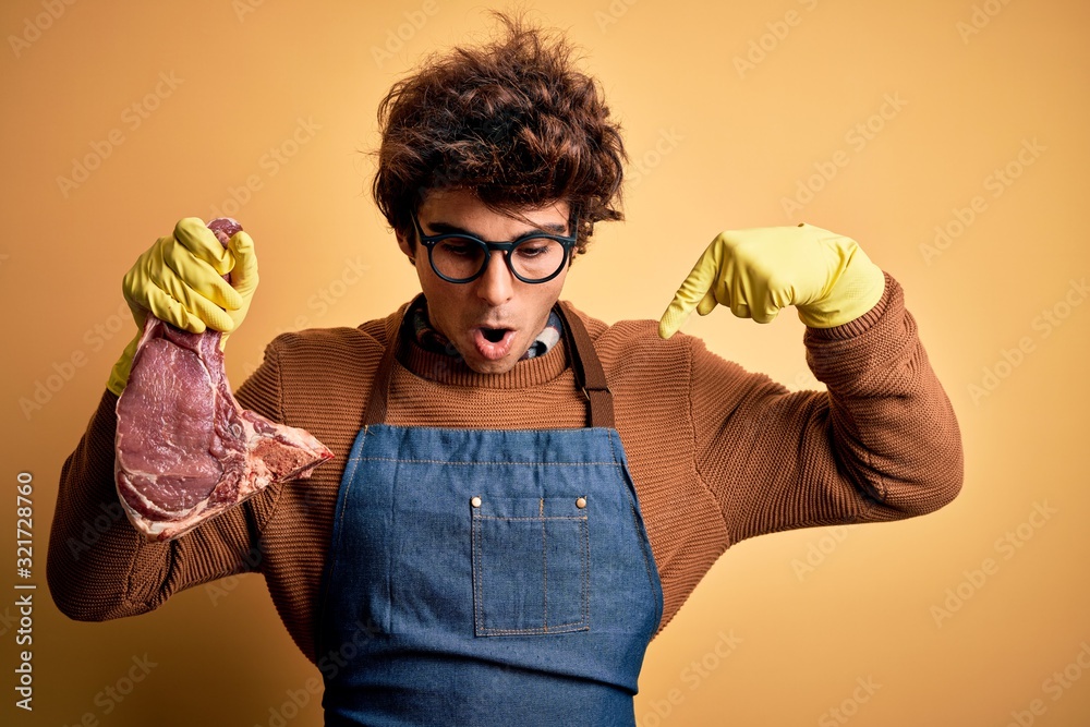 Young handsome butcher man holding meet steak standing over isolated ...