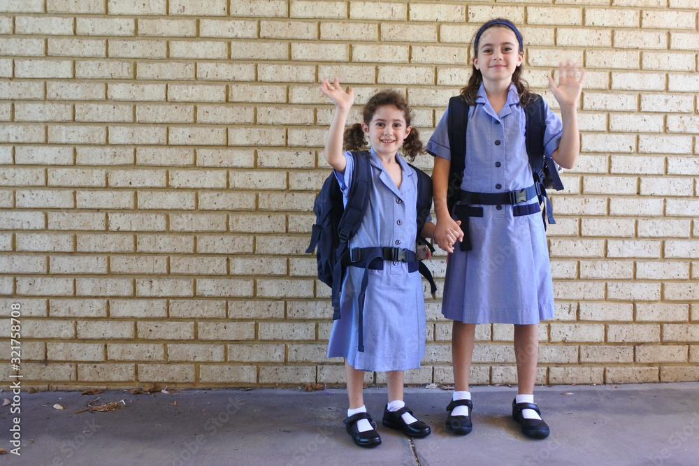 Two happy sisters are waving goodbye before going to school together ...