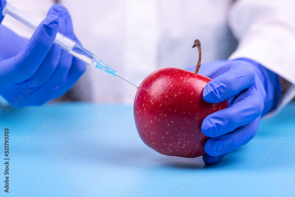 Injection into an apple. A hand in a medical glove with a syringe on a ...