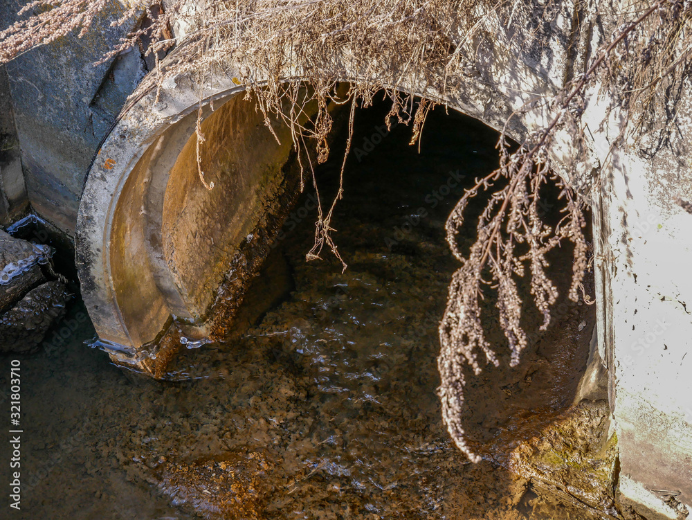 Smelly sewage water flowing trough concrete and iron pipes in a ...