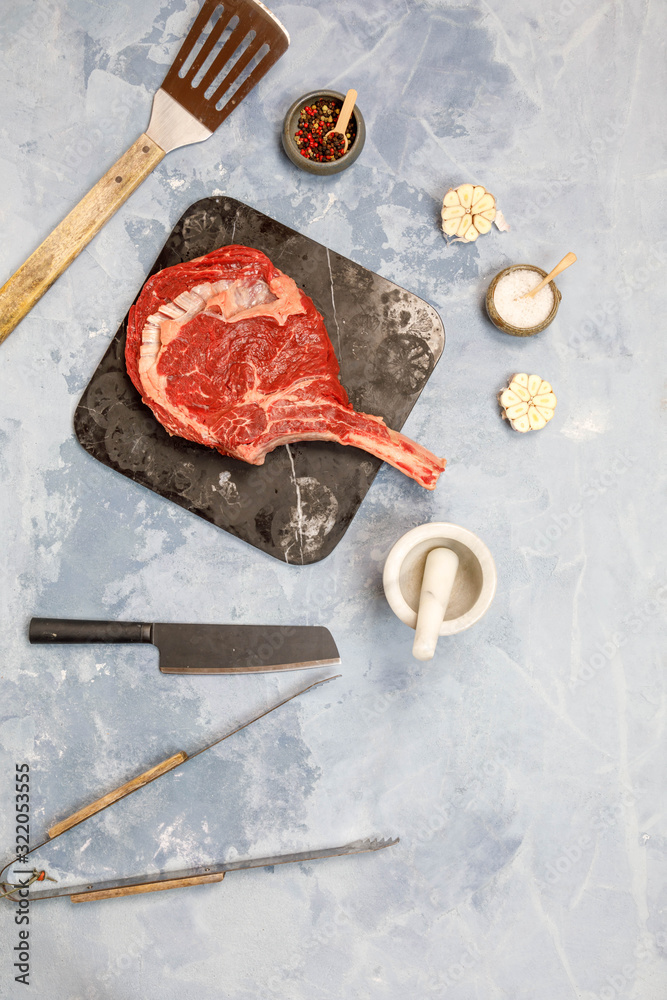 Raw Tomahawk steak on slate tray on light blue concrete background with ...