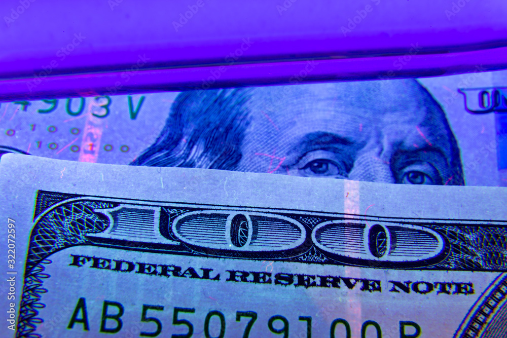 Extreme closeup on dollar banknote under ultraviolet light. Benjamin ...