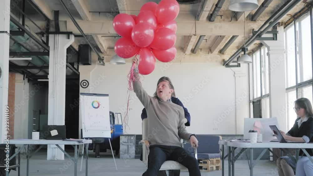 Colleagues congratulate the young manager. They give him red balloons ...