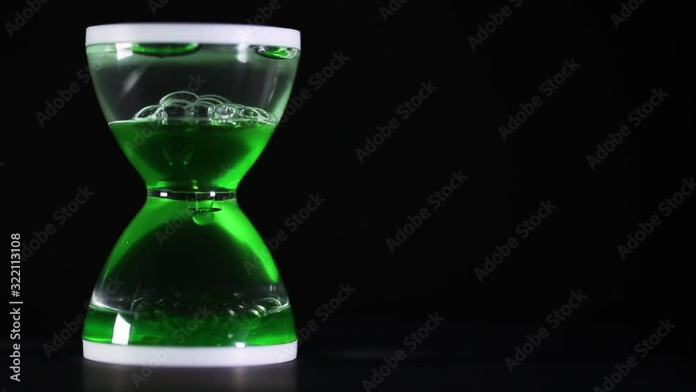 hourglass with green liquid dripping on a black background, leaking ...
