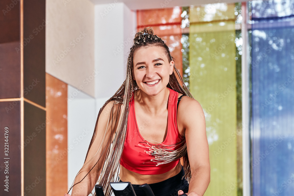 A cheerful young girl working out on a bike simulator at a fitness ...