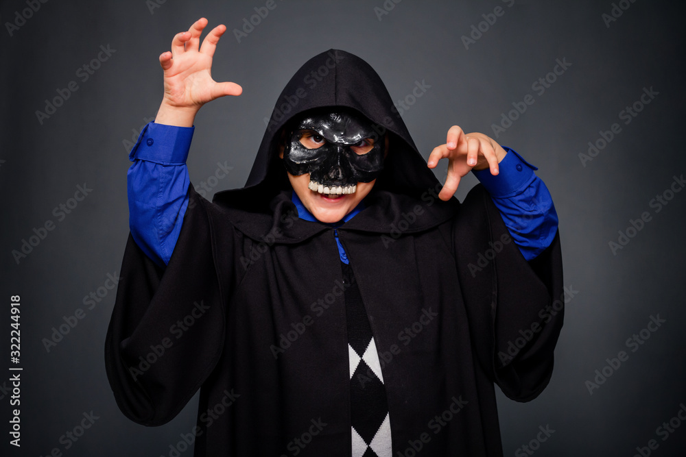 A boy dressed in a black cloak with a hood and a black skull mask ...