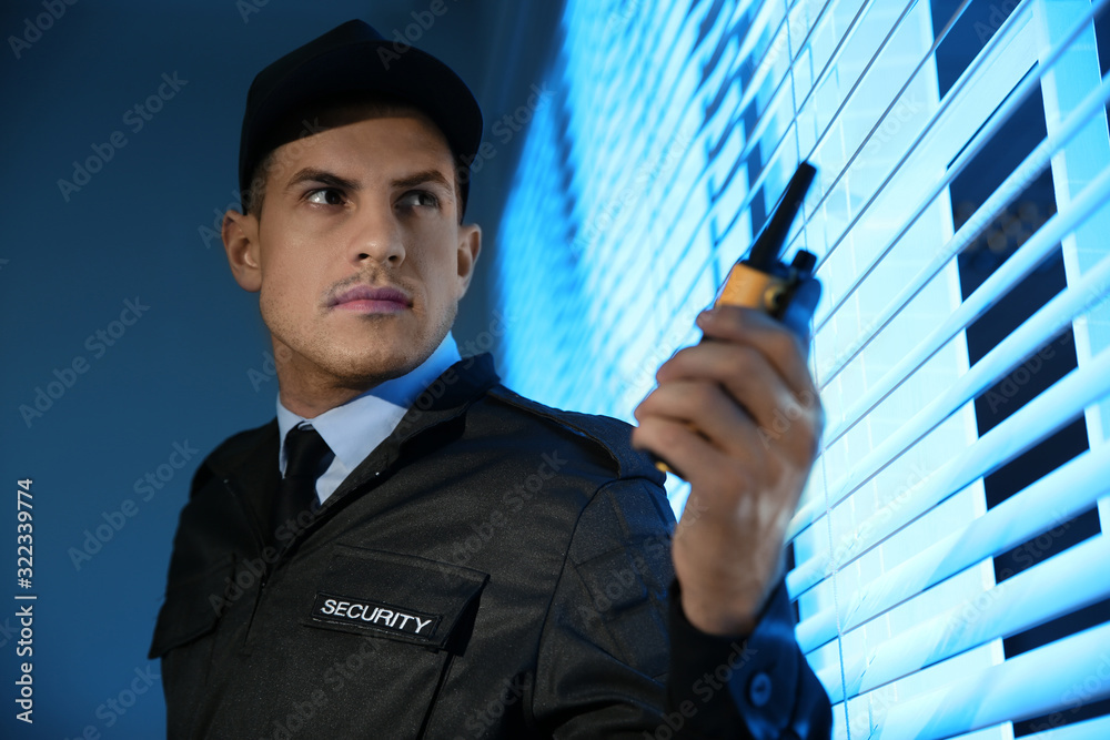 Professional security guard with portable radio set near window in dark ...